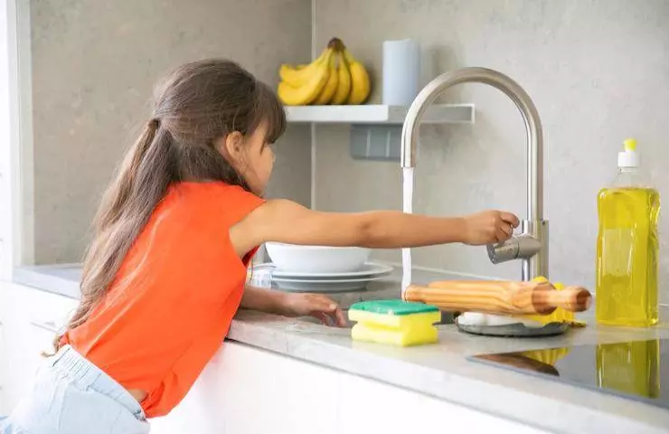A little girl turns on the water in the kitchen